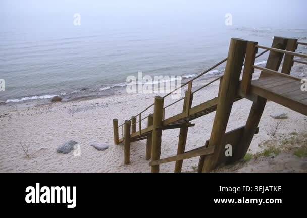 Weathered wooden staircase descends from grassy dune to quiet sandy ...