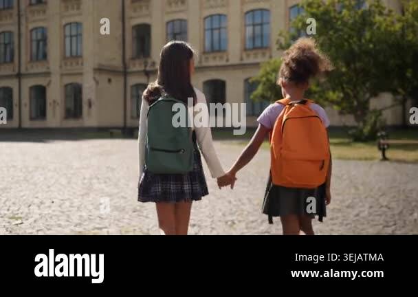Back view two girls schoolgirls with backpacks go to school together ...