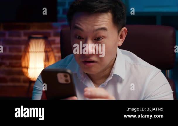 Amazed surprised emotional Asian business man looking in mobile phone ...