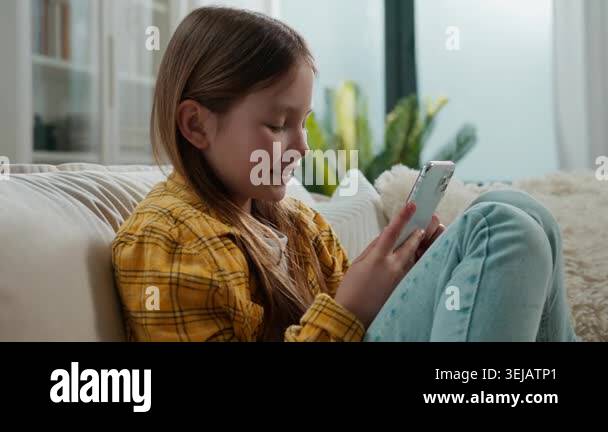 Little teen Caucasian kid girl using mobile phone app smiling satisfied ...