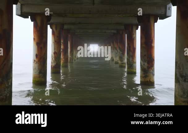 Weathered rusted metal pillars of pier rise vertically from calm sea ...