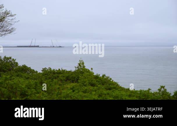 Serene coastal landscape featuring calm gray sea under overcast sky ...