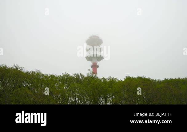 Tall red and white lighthouse emerges faintly through thick fog behind ...