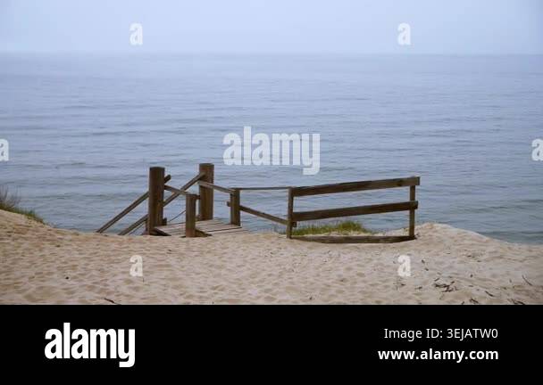 Quiet sandy beach with wooden railing steps leading to calm sea water ...