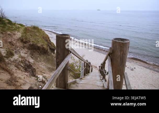 Weathered wooden stairway leads from grassy dune down to tranquil sandy ...