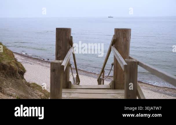 Weathered wooden staircase descends to pebbled sea shore with gentle ...