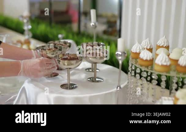 Waiter in gloves arranging chocolate mousse desserts in silver bowls at ...