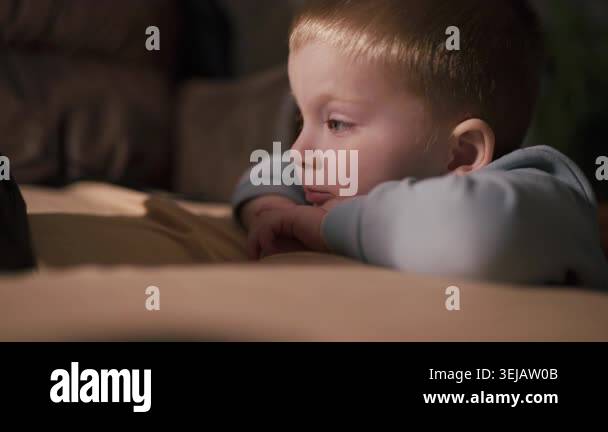 Little boy watching cartoons on digital screen in a dark cozy room ...
