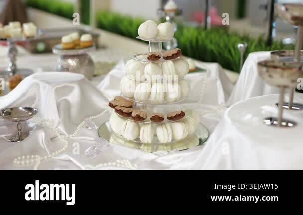 Catering worker arranging white macarons and shell cakes on a tower ...