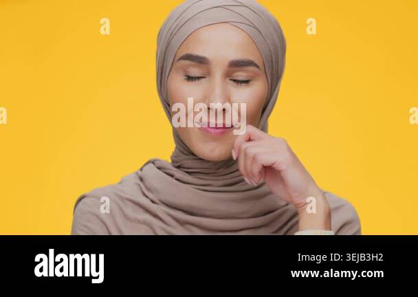 A woman is standing in front of a bright yellow backdrop. She wears a ...