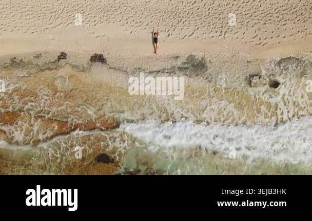 Woman lying on sandy beach near foamy sea waves from top aerial view ...