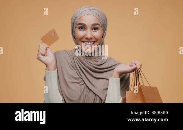 A woman dressed in a hijab smiles while holding shopping bags in one ...