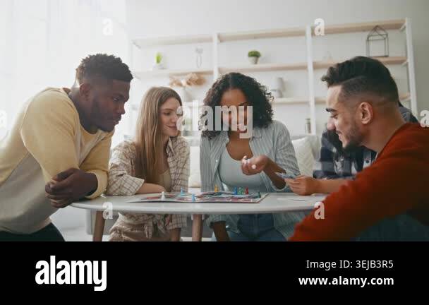 A group of four friends gather around a table for game night. They are ...