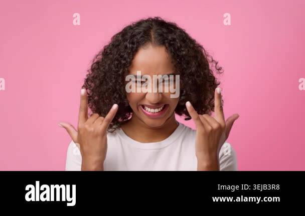 A young woman with curly hair makes a rock gesture with her hands. She ...