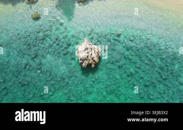 Single rock in crystal clear shallow turquoise water near shore Stock ...