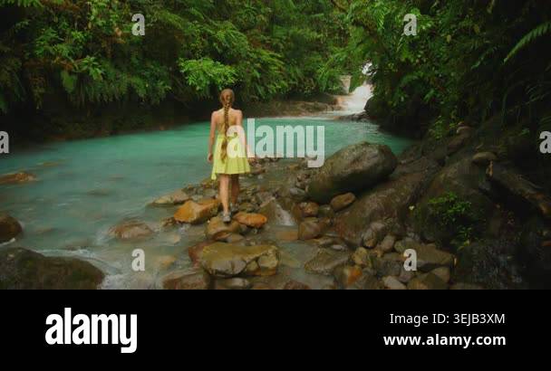 Woman walking across rocky stream toward Blue Falls pool on a vibrant ...