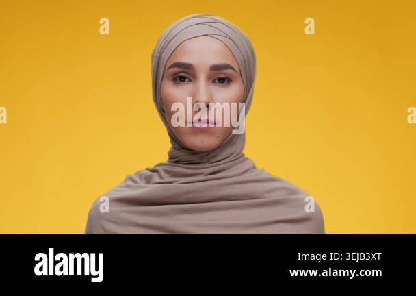 A woman with a hijab stands against a bright yellow background. She has ...