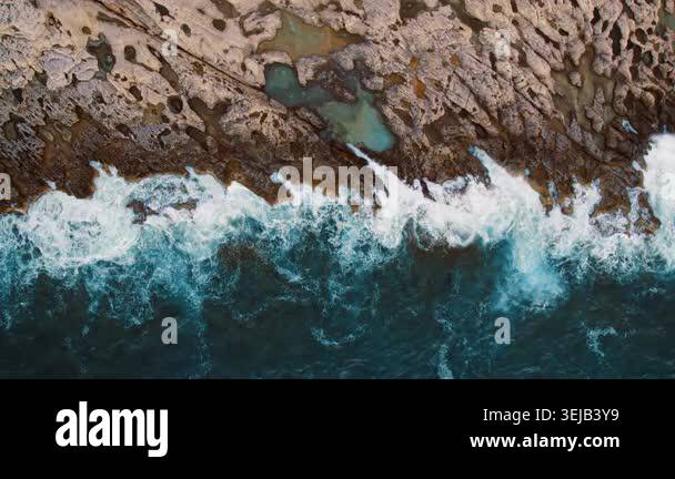 Waves crashing onto a textured rocky shoreline with tide pools from ...