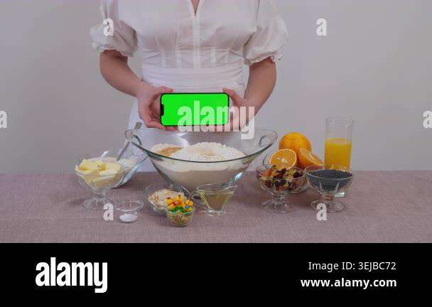 young female baker holds smartphone with green screen while preparing ...