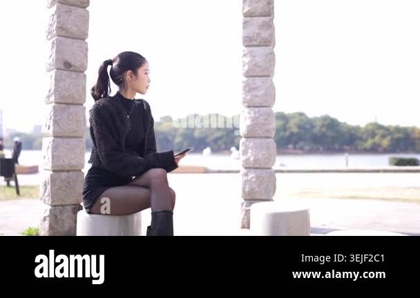 Woman sitting near stone pillar holding phone Stock Video Footage - Alamy