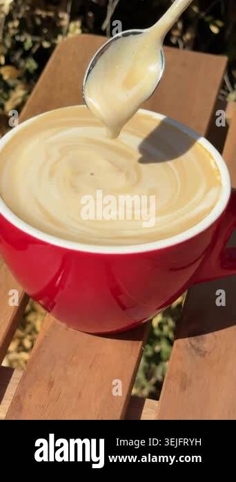 Stirring creamy coffee in cup with spoon in a cozy setting. red cup, in ...