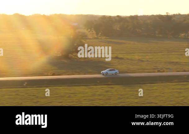 Cars driving along a straight road through open land, evening light ...