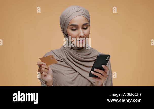 A woman holds a phone in one hand and a card in the other while looking ...