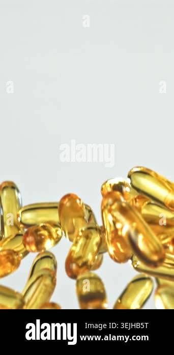 Golden capsules falling against white background, omega oil softgel ...