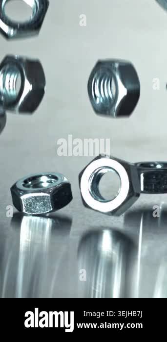 Closeup chrome nuts falling and bouncing on reflective table, product ...