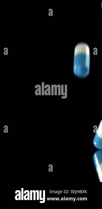 Blue antibiotic capsules scattered on glossy black surface Filmed on a ...