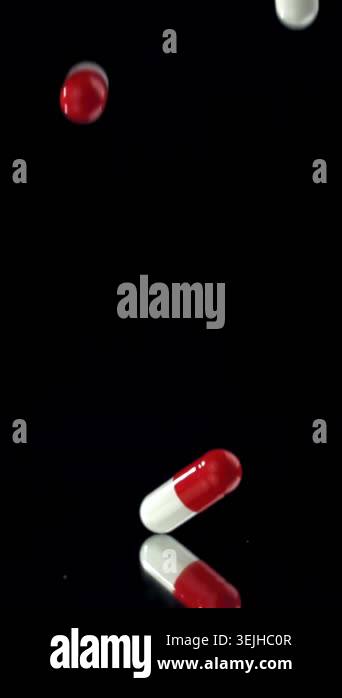 Red white capsules dropping against black backdrop reflective surface ...