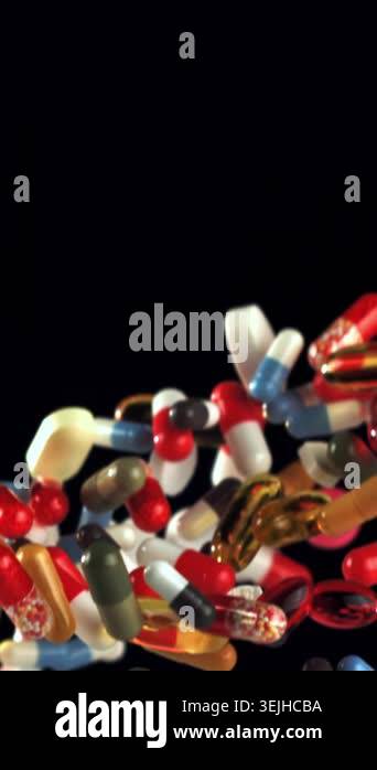 Assorted capsules and tablets tumbling across black background, mixed ...