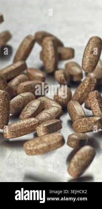 Brown herbal tablets scatter on metal countertop, compressed granules ...