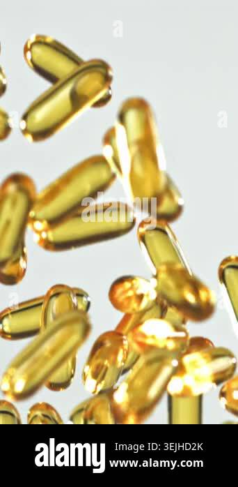 Golden softgel capsules falling against white backdrop, studio Filmed ...