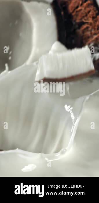 Pieces of coconut fall into the milk with splashes. Filmed on a high ...