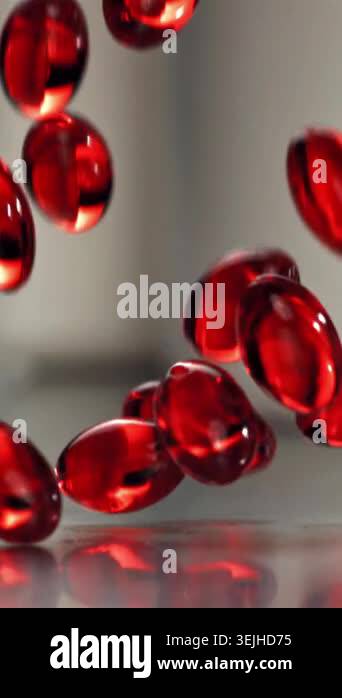 Red softgel capsules on reflective table, closeup next to blurred ...