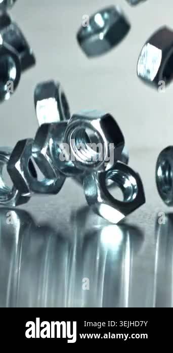Falling metal nuts cascade across reflective surface, dynamic tumble ...