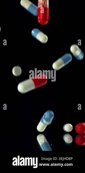 Assorted pills and capsules raining on black reflective surface Filmed ...