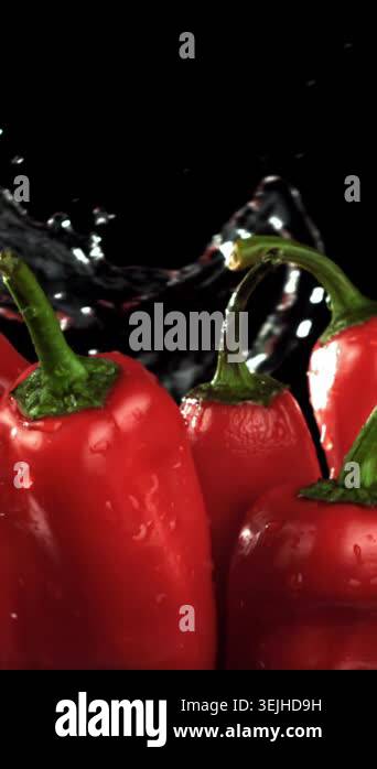 Red chili cluster hit by water splash on black background, dynamic ...