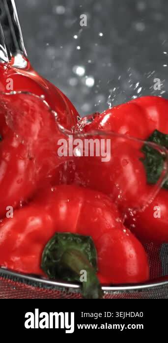 Kitchen closeup red bell peppers rinsed in metal strainer with pouring ...