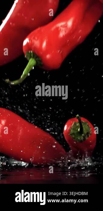 Red chilies splashing on black background, glossy skin, high speed ...