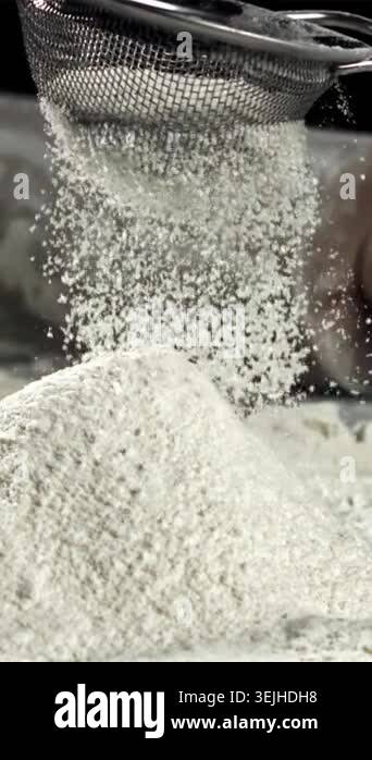 The flour is sifted onto a mound with flour. Filmed on a high-speed ...