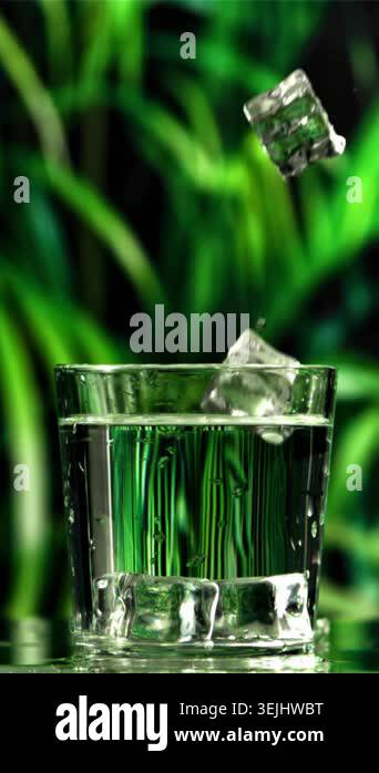 Ice cubes with splashes fall into a glass of water. Against a backdrop ...