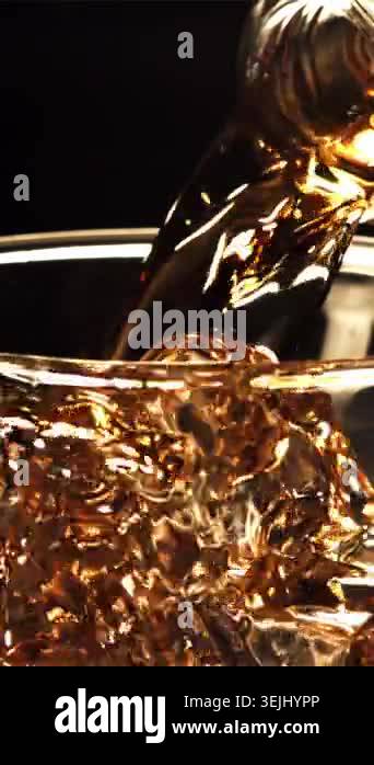 Whiskey is poured into a glass of ice. On a black background. Filmed on ...