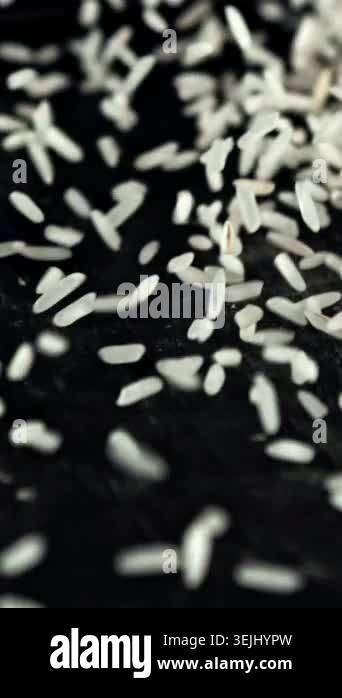 A pile of uncooked rice falls on the table. On a black background ...