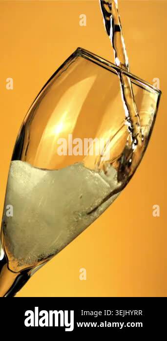 Stream of champagne pours into a glass of air bubbles. On a yellow ...