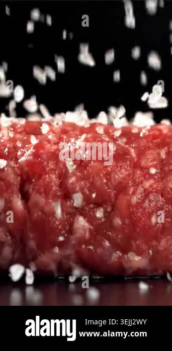 The cook sprinkles salt on the meat burger. Filmed on a high-speed ...