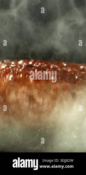 A beef burger falls into a hot pan with a splash of oil. Filmed on a ...