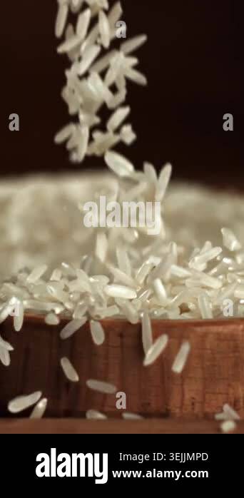 White rice falls into a wooden bowl. Filmed on a high-speed camera at ...