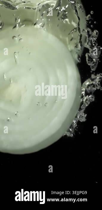 Sliced onion falling into water on black background. Filmed on a high ...